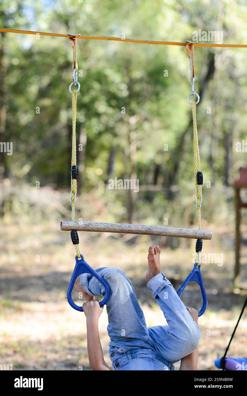 A child in jeans plays on a hanging rope swing set in a forested Stock ...