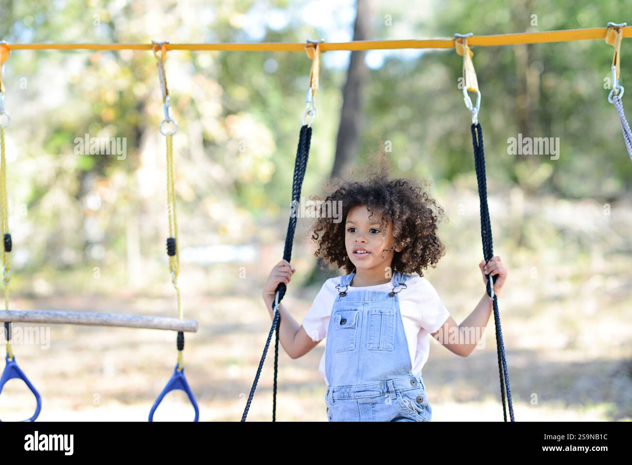 A child in overalls holds onto ropes on a playground swing outdo Stock ...