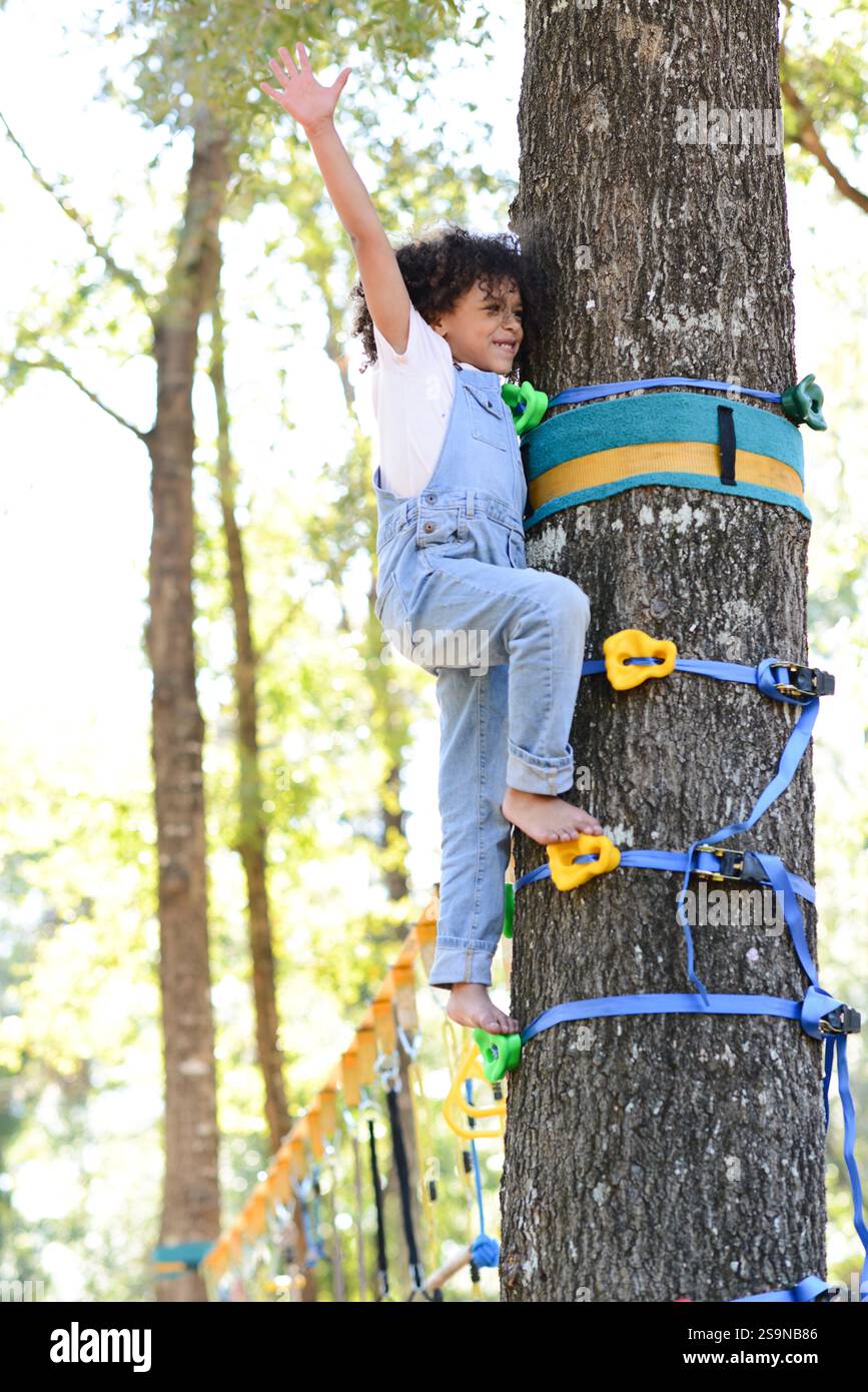 Child climbing a tree with colorful grips, raising one arm in jo Stock ...