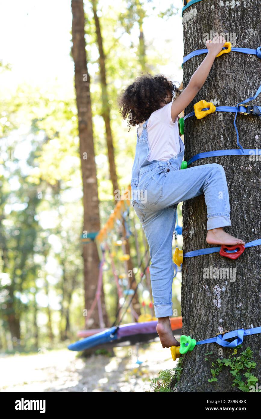 Child climbing a tree using colorful grips, barefoot, in a playf Stock ...