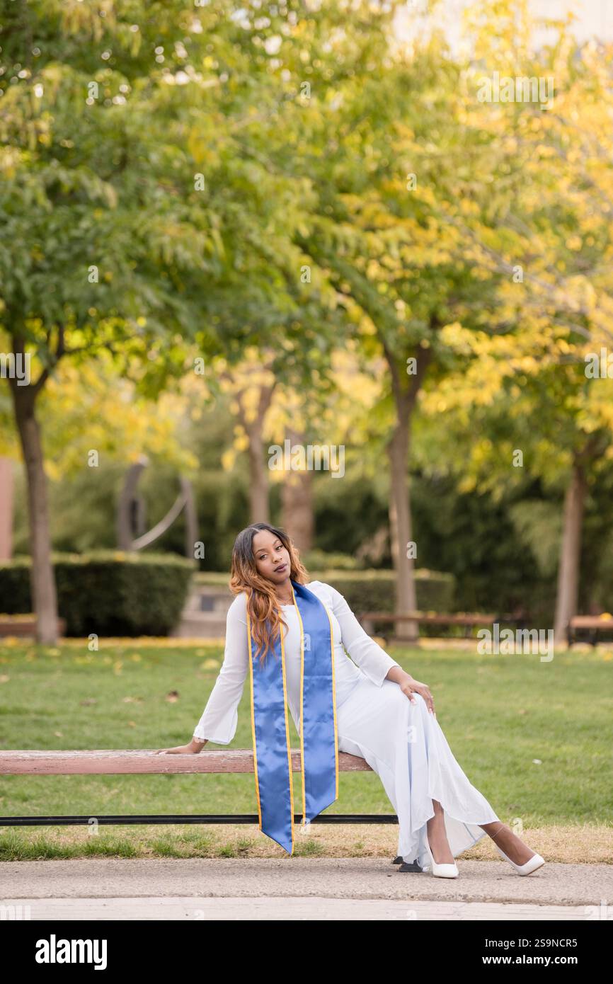 Woman graduate wearing sash sitting on a bench Stock Photo - Alamy