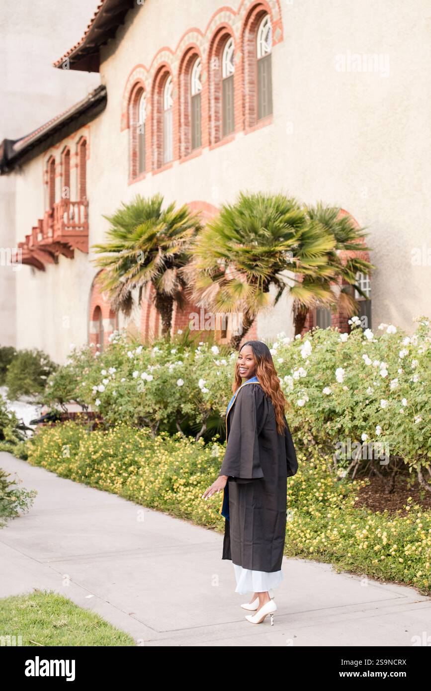 Woman walking away in graduation gown in front of school Stock Photo ...