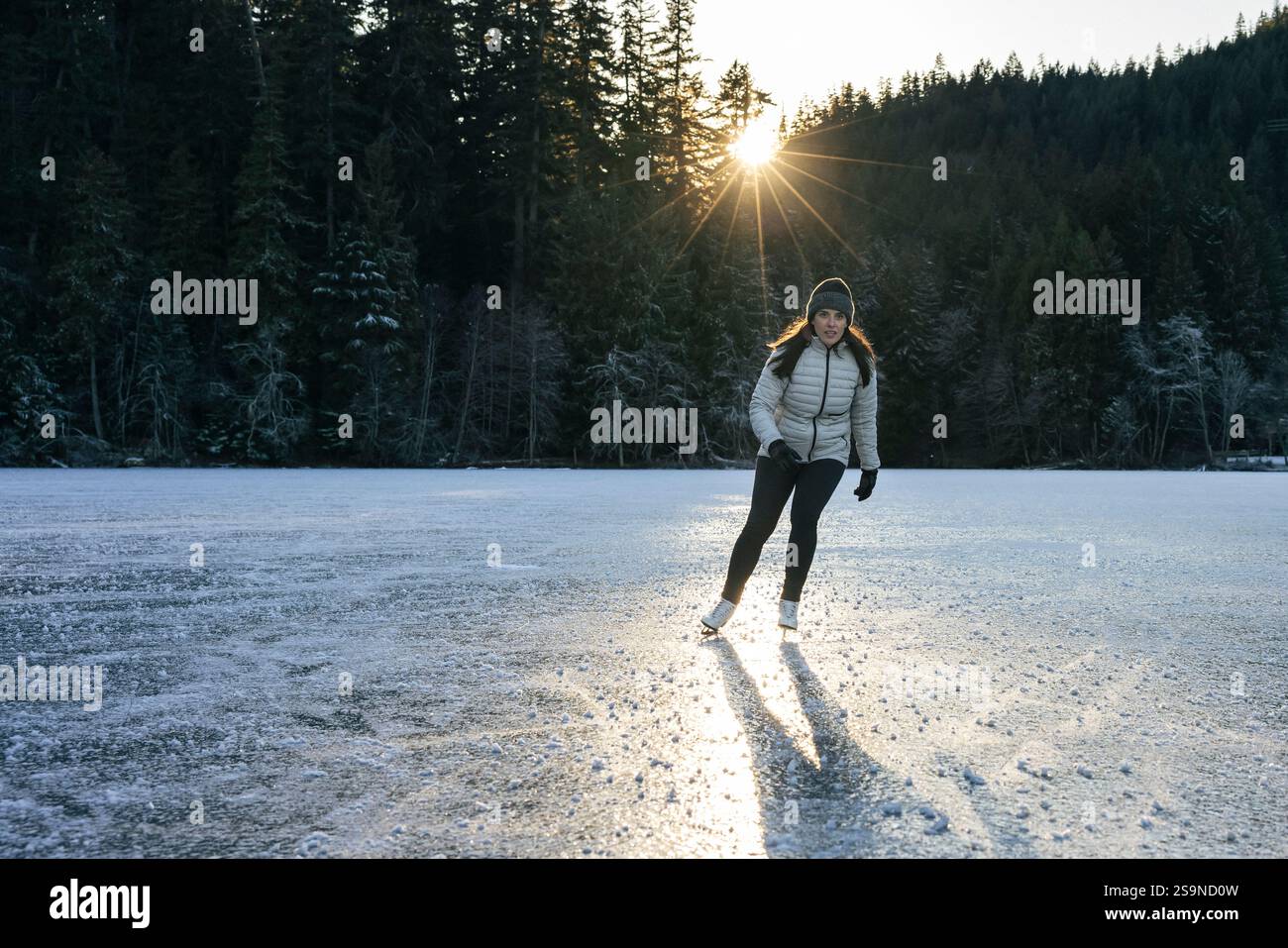 Female ice skater gliding on a reflective frozen lake at sunset Stock ...