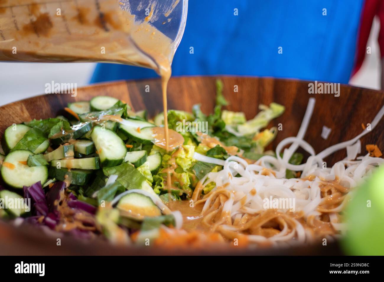 Peanut salad dressing being poured onto noodle and vegetable salade ...