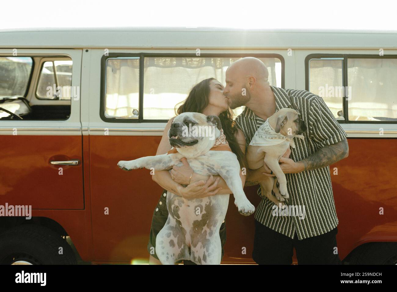 Couple shares a smooch by their van, holding their dogs Stock Photo - Alamy