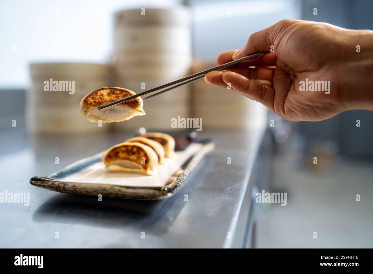 Close-up of a hand using chopsticks to pick up a grilled dumpling in a ...