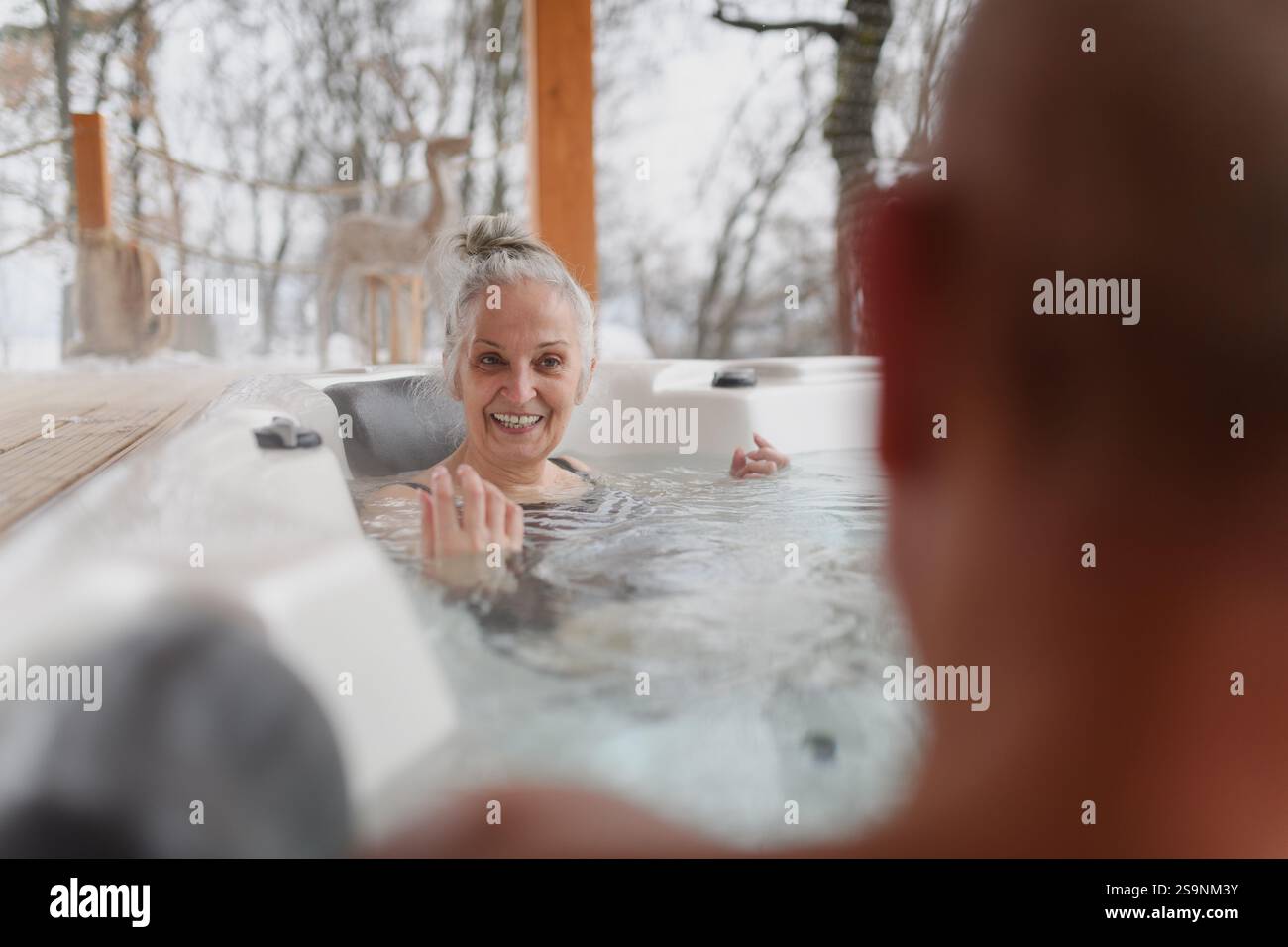 Bathing in hot tub during cold winter day. Older woman sitting in water ...