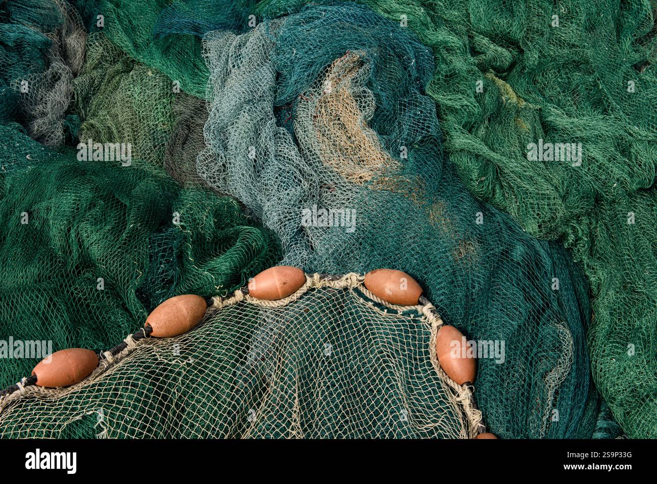 A tangle of large, green and blue fishing nets and buoys, laying on a ...