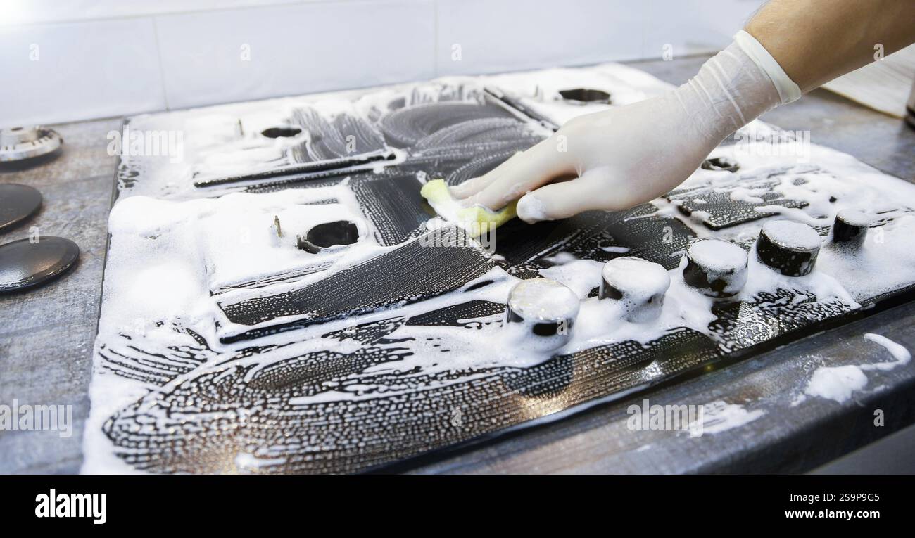 Gloved hand wiping a soapy stove with a cleaning sponge in a kitchen ...