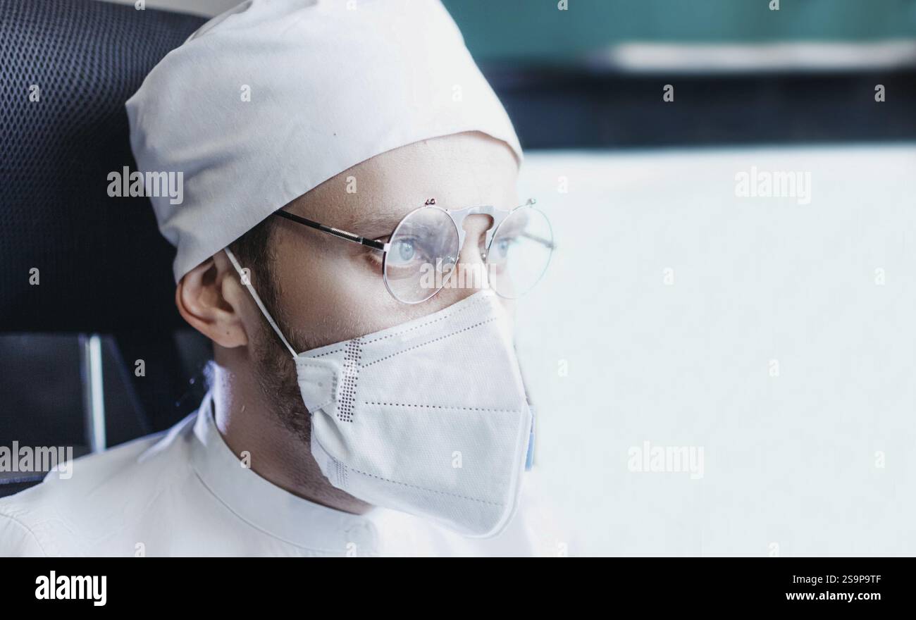 A masked surgeon with a cap, eyes focused, under bright light in a ...