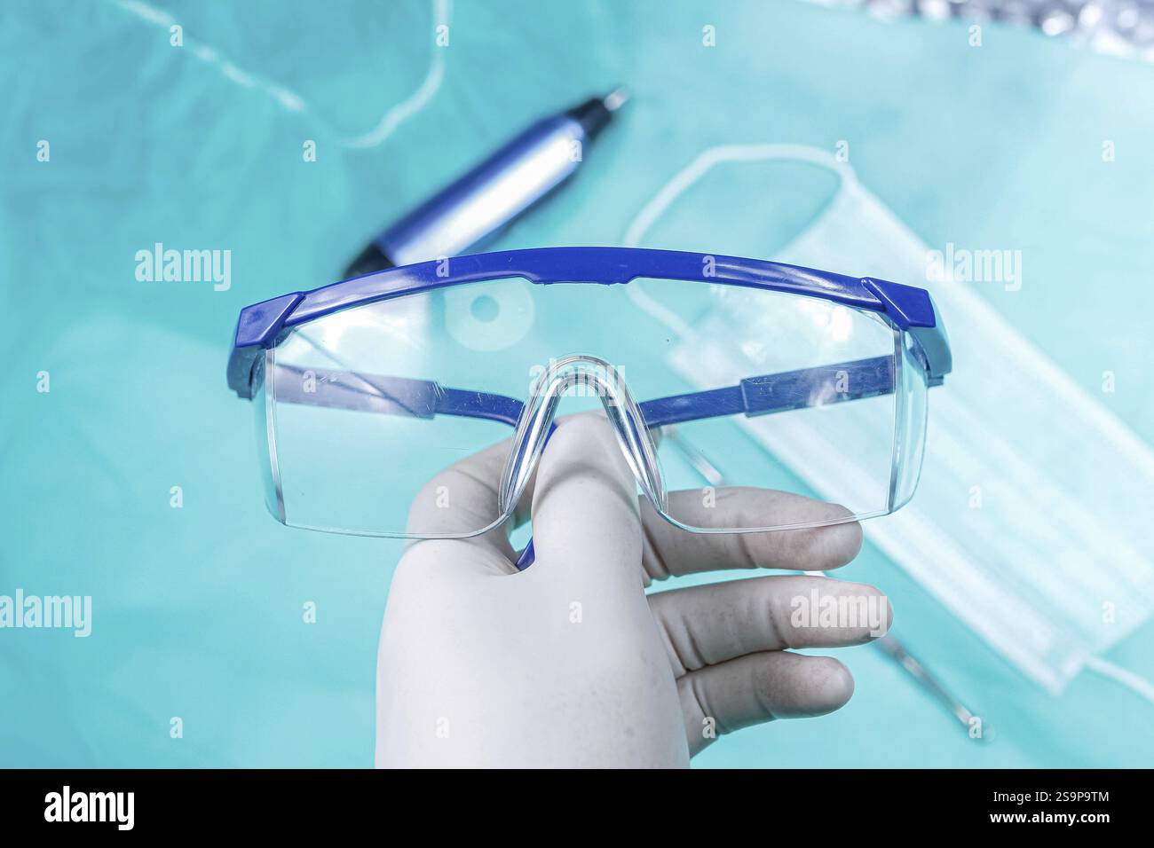 Hand holds protective eyewear over a blue background with medical tools ...