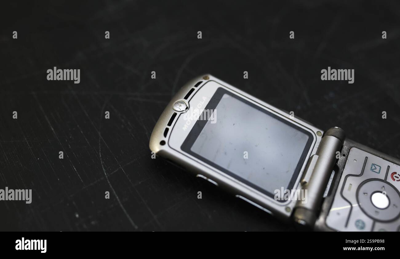 Silver flip phone with visible screen on a dark textured background ...