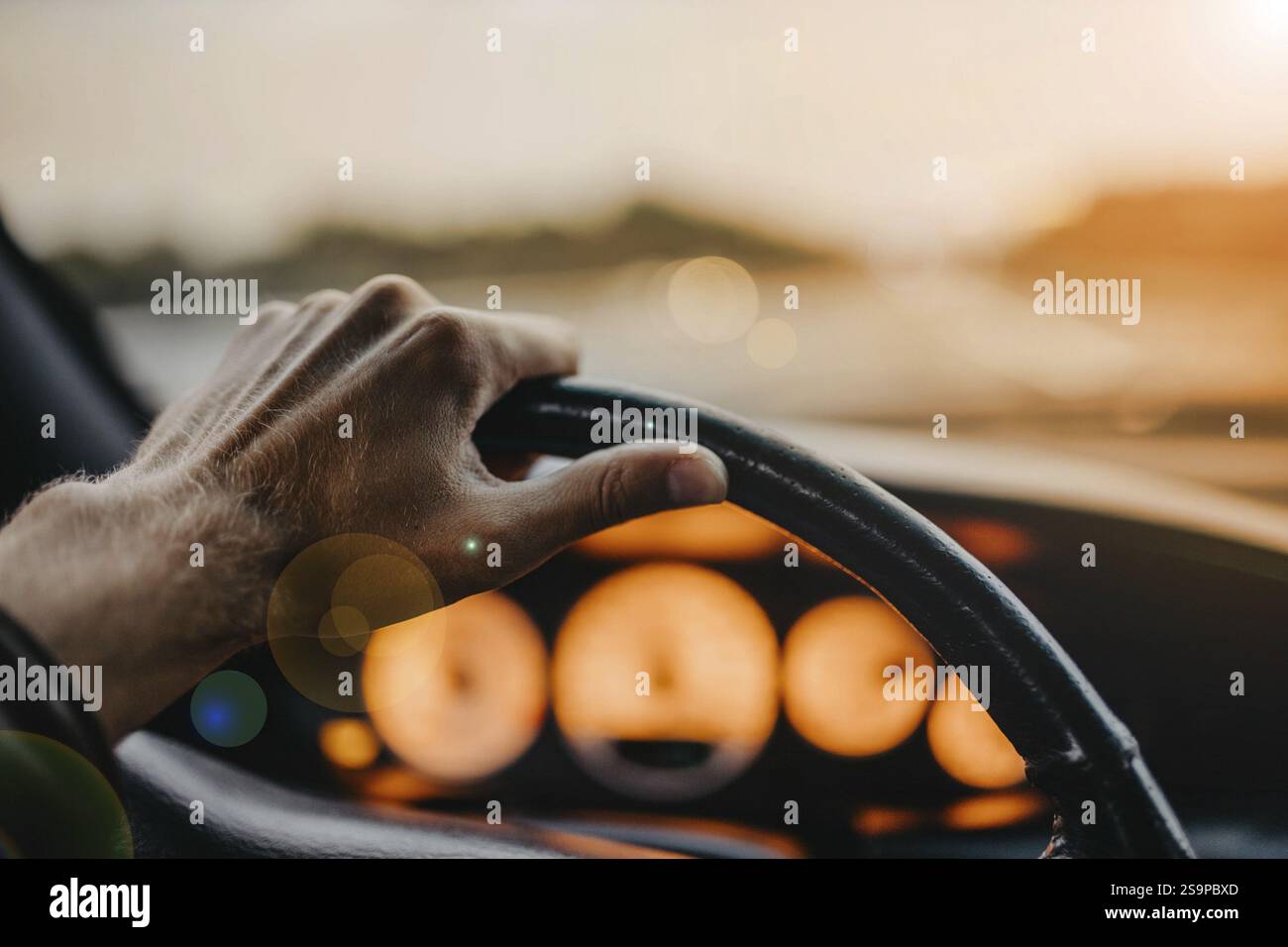 A hand on the steering wheel during sunset with golden light ...