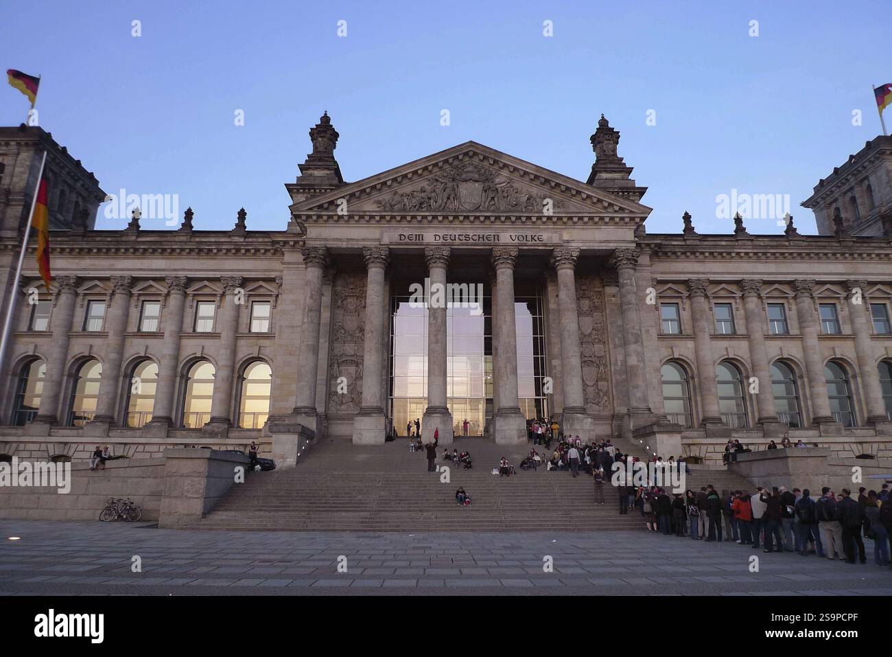 The Reichstag building at dusk, people standing on the steps in front of the impressive ...