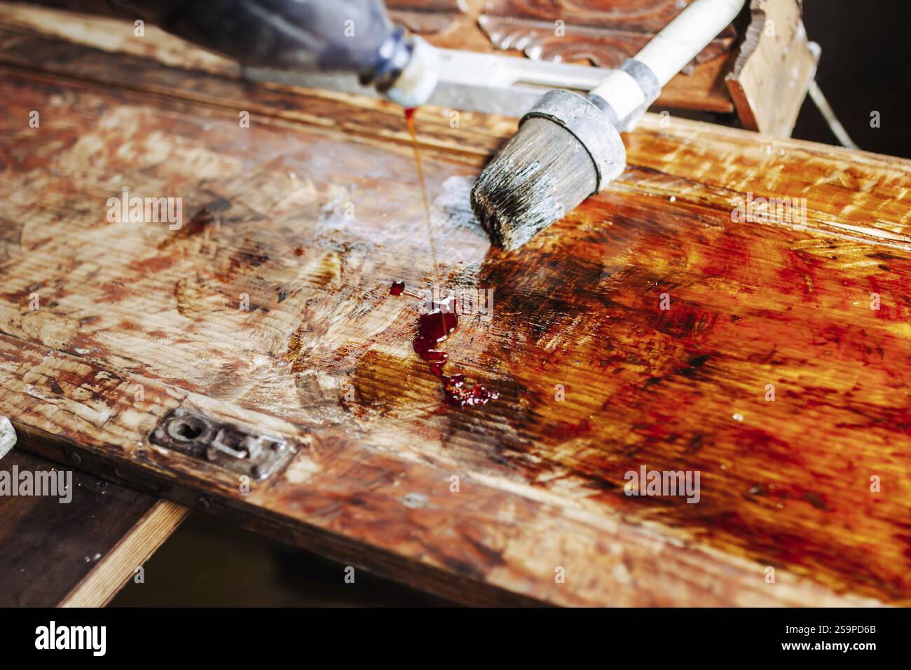 Applying red stain to wood with a brush, creating a glossy, textured ...