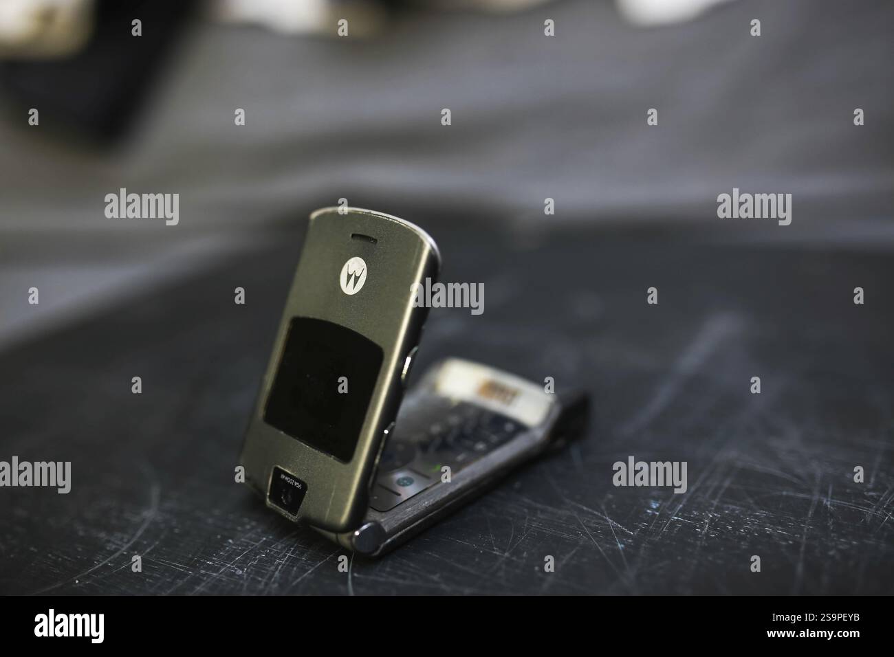 A half-open Motorola flip phone displayed on a black scratched surface ...