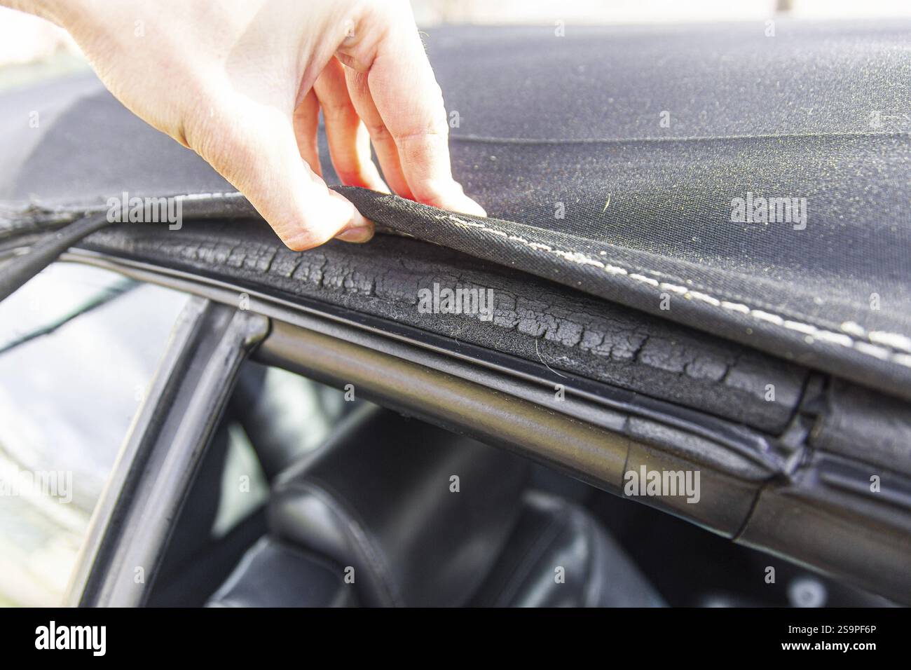 Hand examining the worn edge of a black convertible roof in bright ...