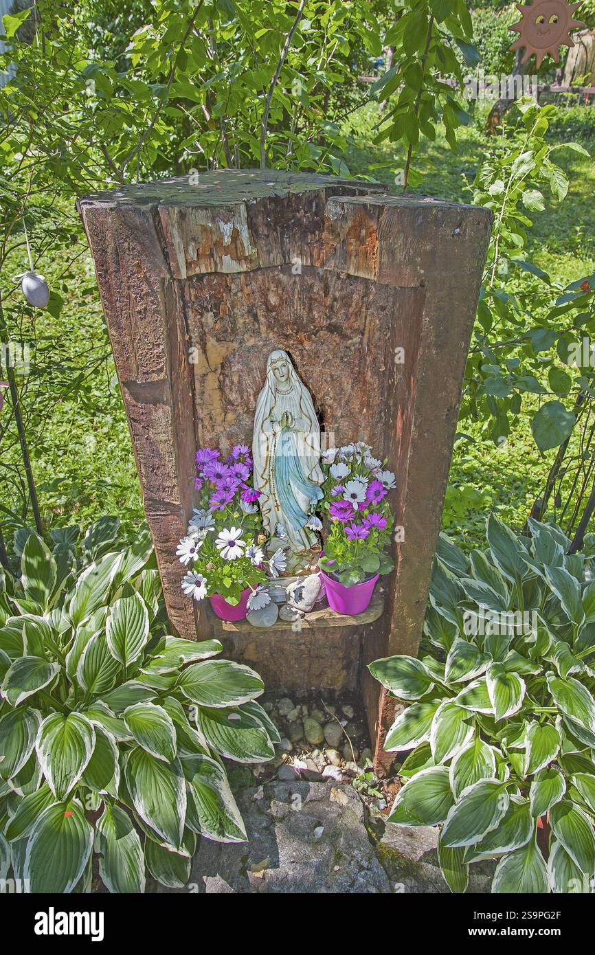 Figure of the Virgin Mary in a tree stump with floral decoration at the ...