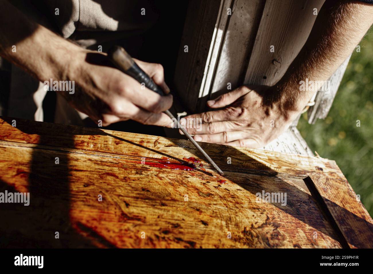 Person chiseling a wooden surface, hands casting shadows in sunlight ...
