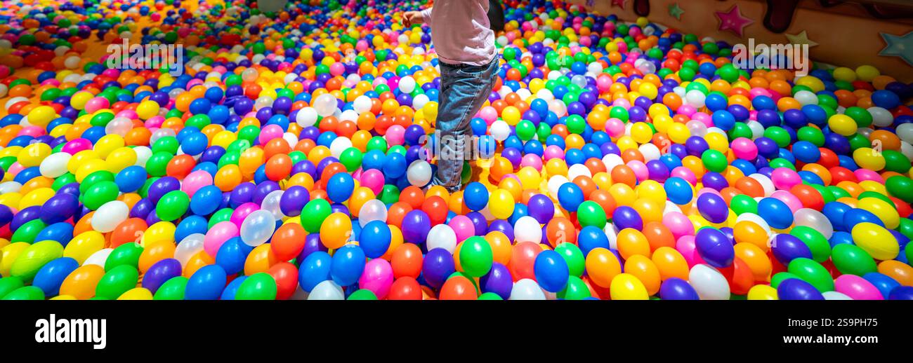 A playful child walking through a colorful ball pit in an indoor ...