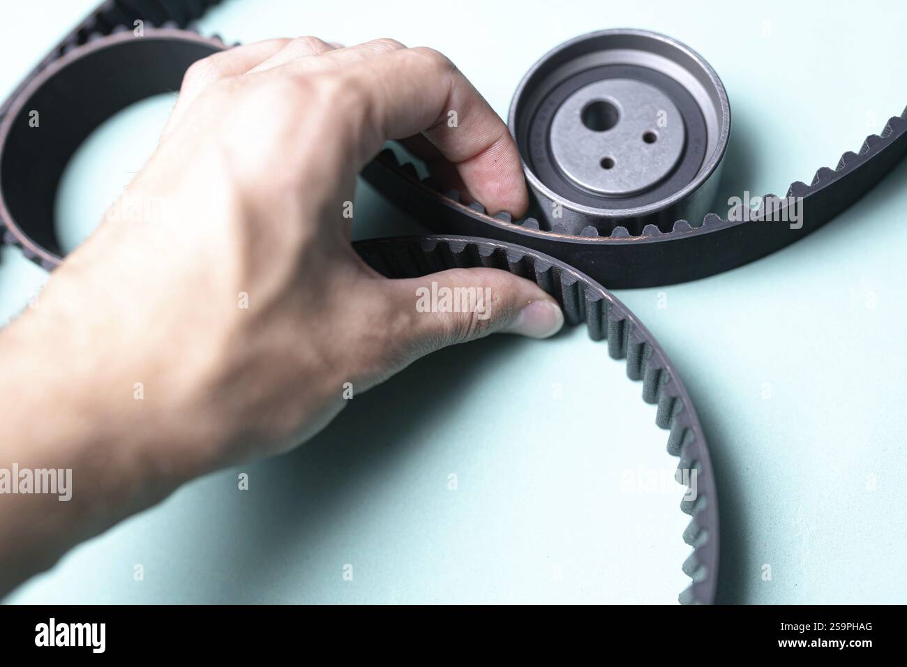 Hand adjusting a timing belt with gears on a mint green surface Stock ...