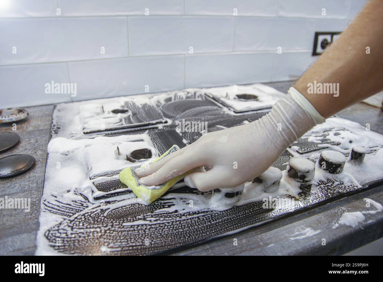 Gloved hand cleaning a soapy stove with a cleaning sponge in a kitchen ...