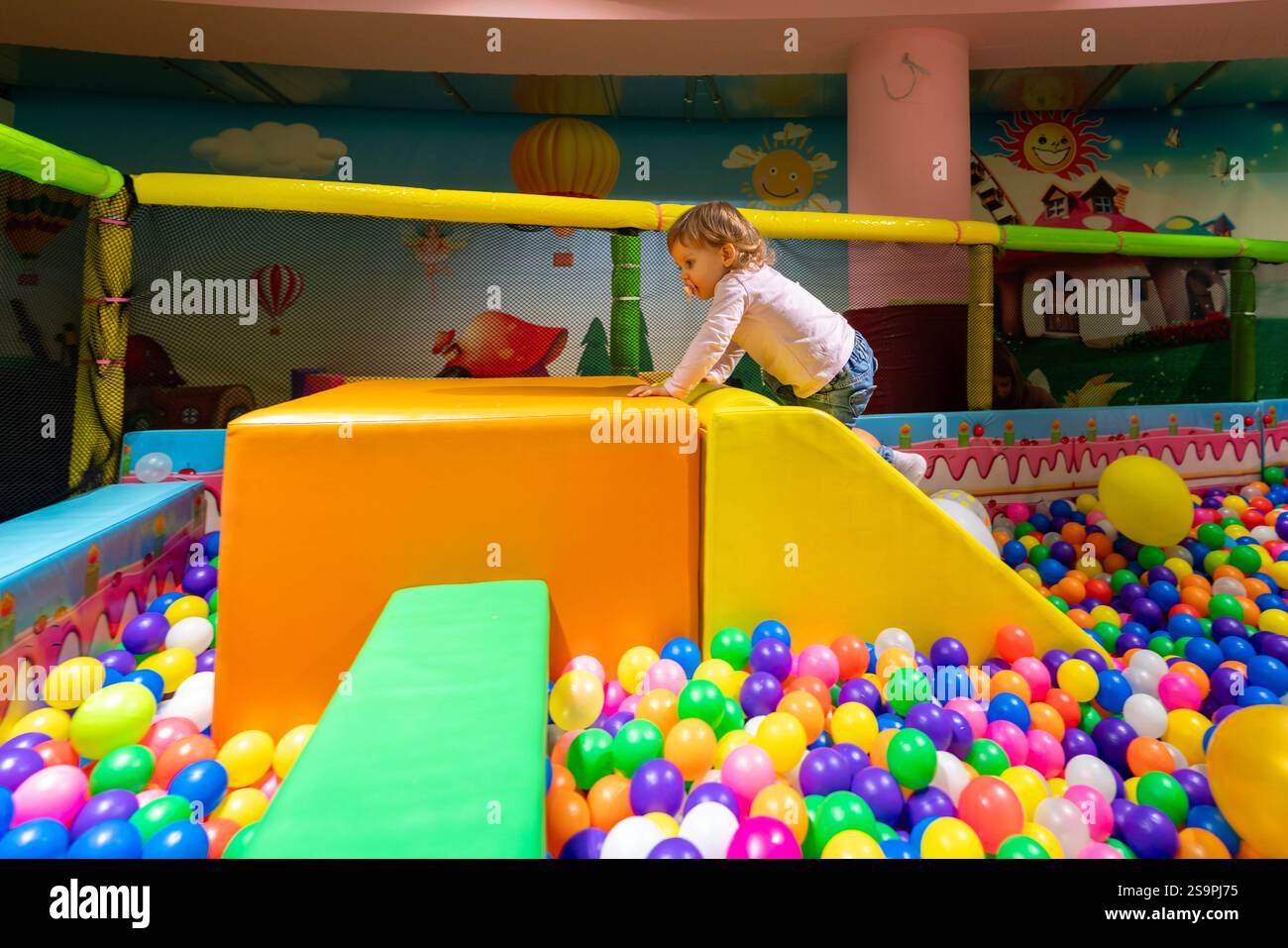 A playful child climbing a soft slide in a colorful ball pit at a ...