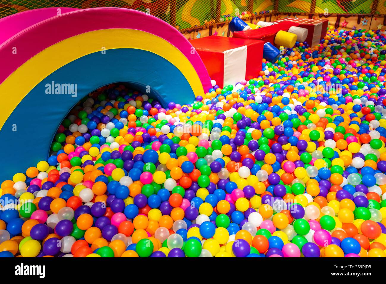 A colorful ball pit with a rainbow-shaped soft structure in a vibrant ...