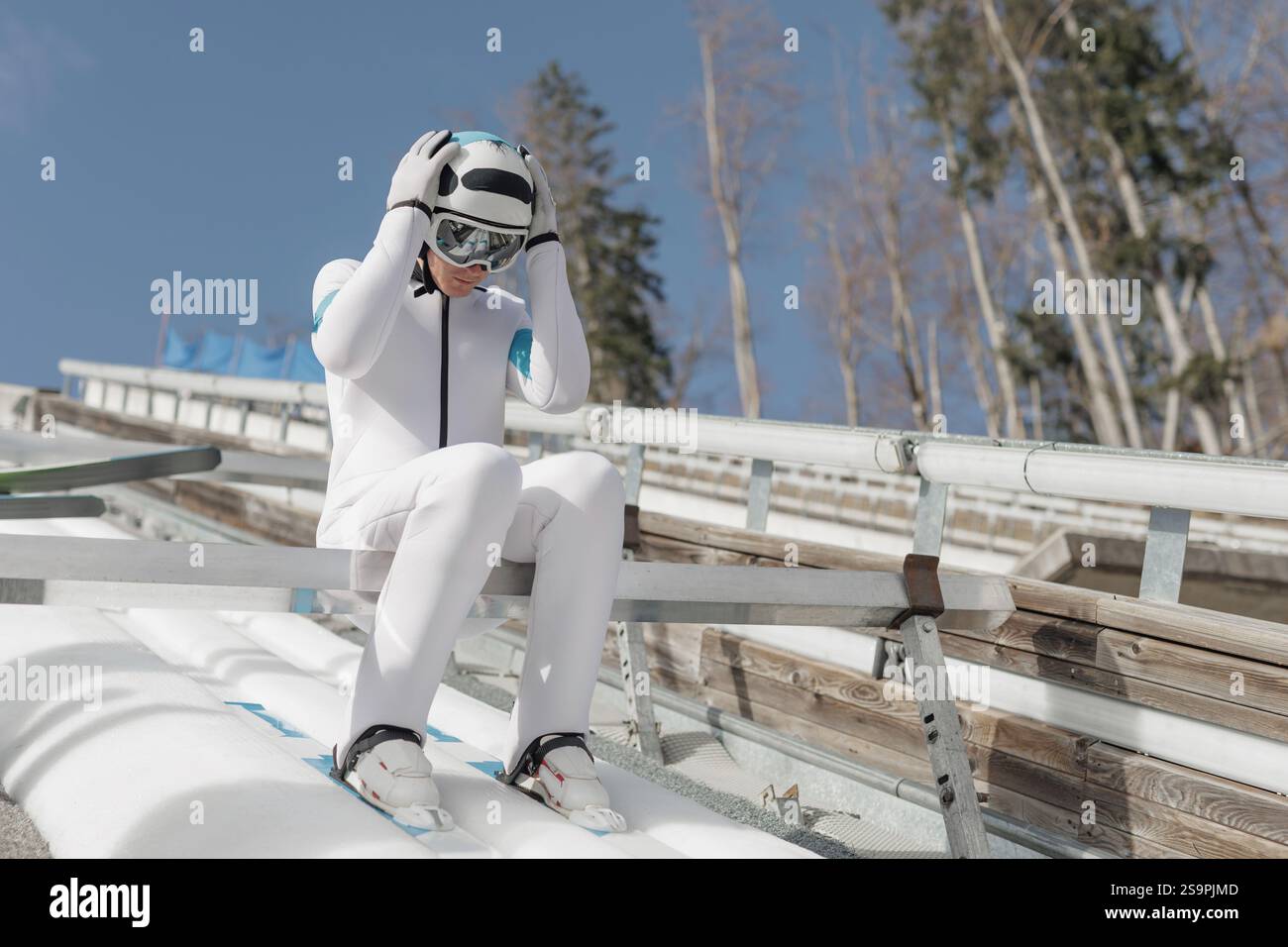 Ski jumper sitting on a bar at a start gate, calming nerves with deep ...
