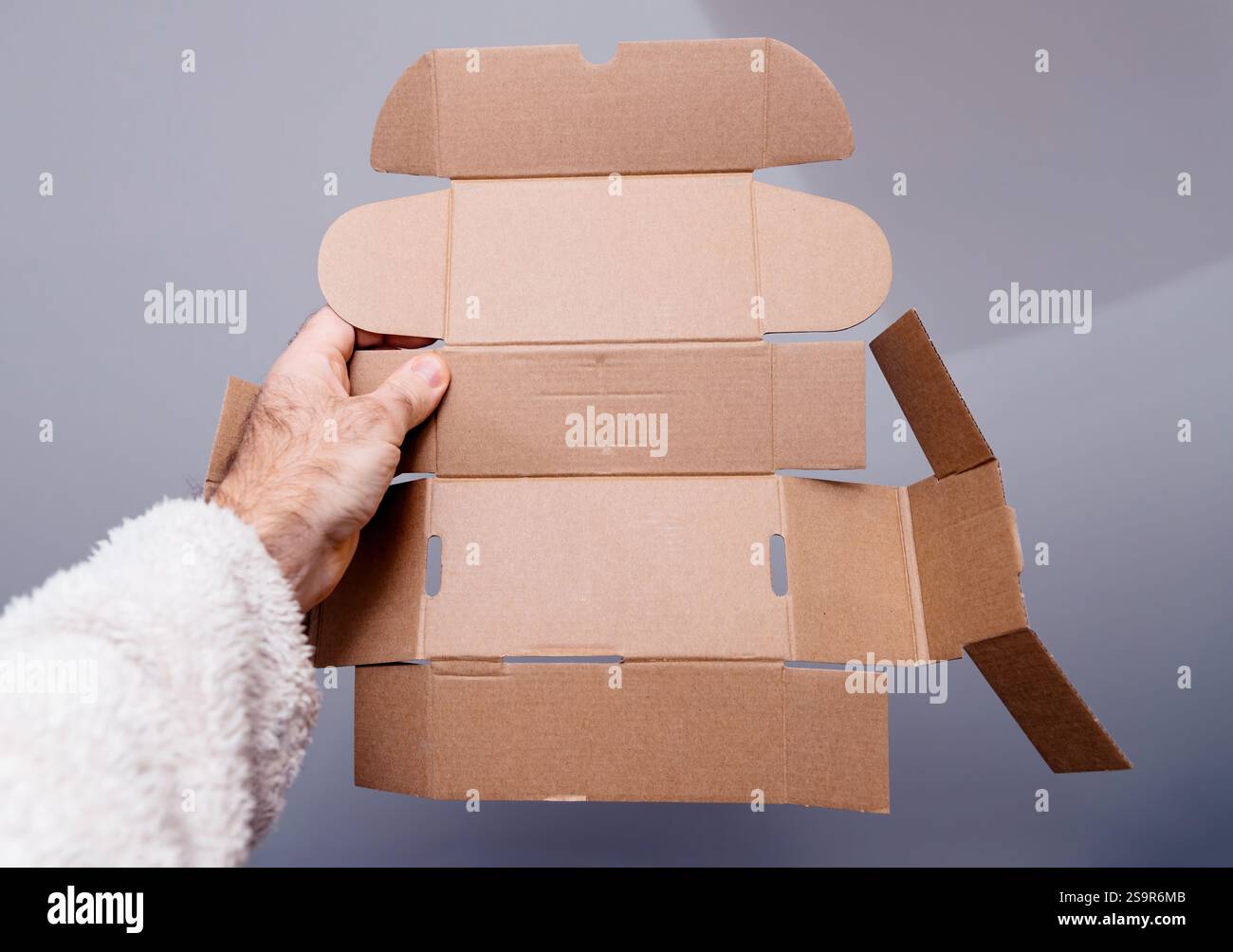 A hand holding a flattened cardboard box design, showing its foldable ...