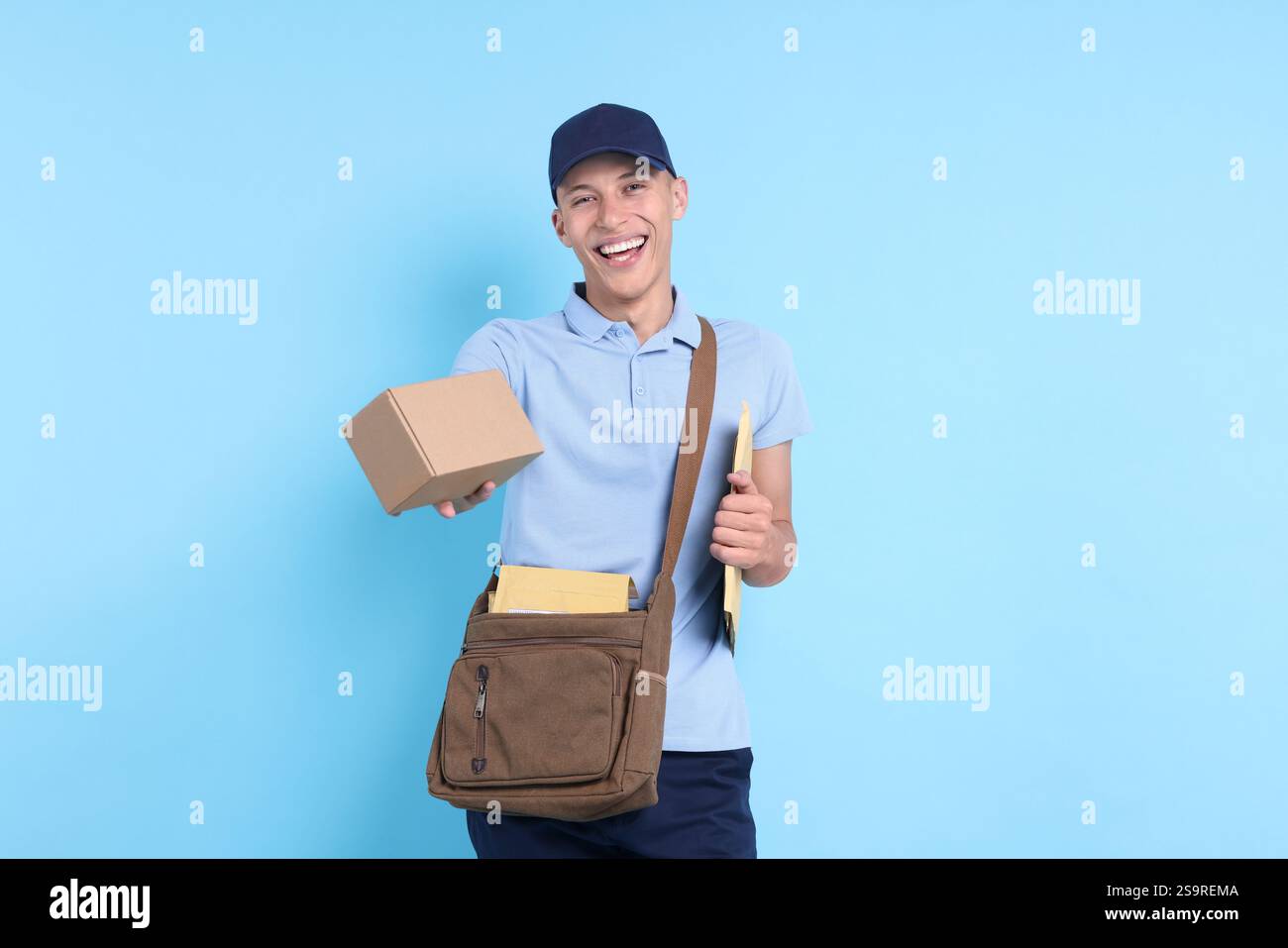 Happy postman with bag, envelopes and parcel on light blue background ...