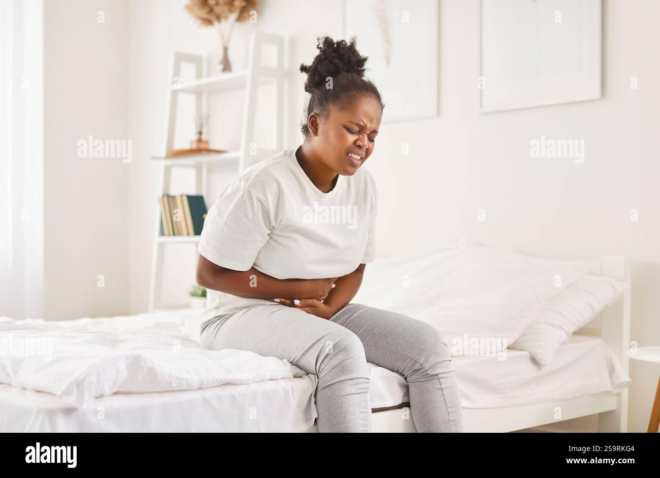 Sick african american woman sitting on bed putting hands on belly ...