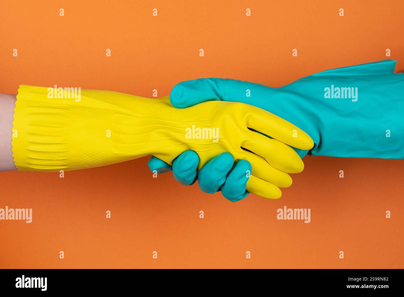 Two hands wearing yellow and blue rubber gloves shake hands against a ...