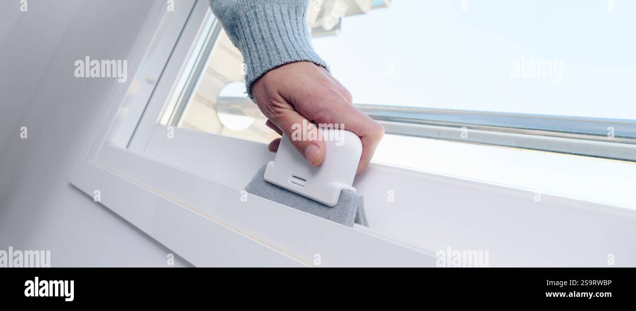 a man cleans the grooves of a white sliding window frame using a ...