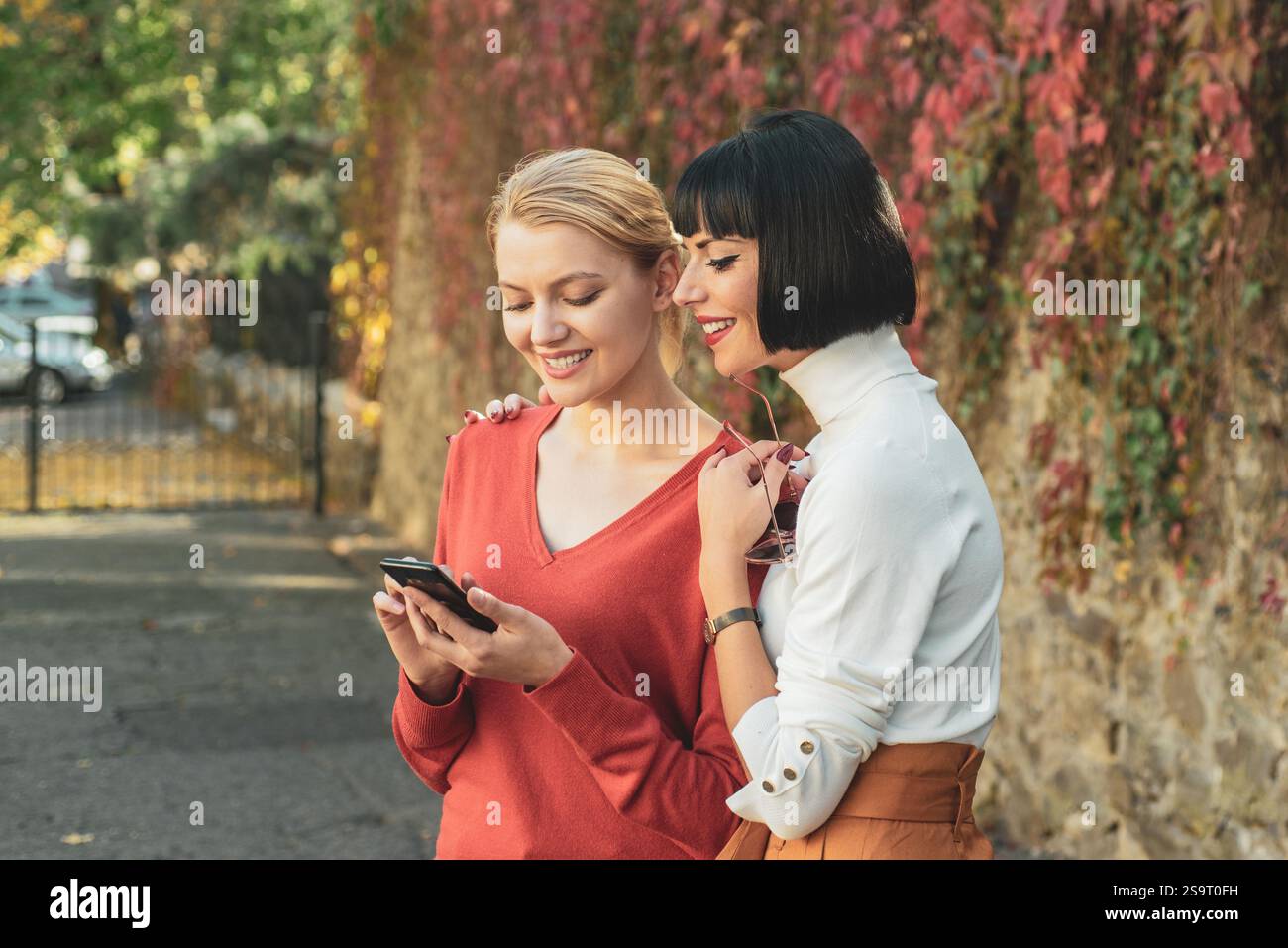 Two excited girls using mobile phones in park. Girls friends using ...