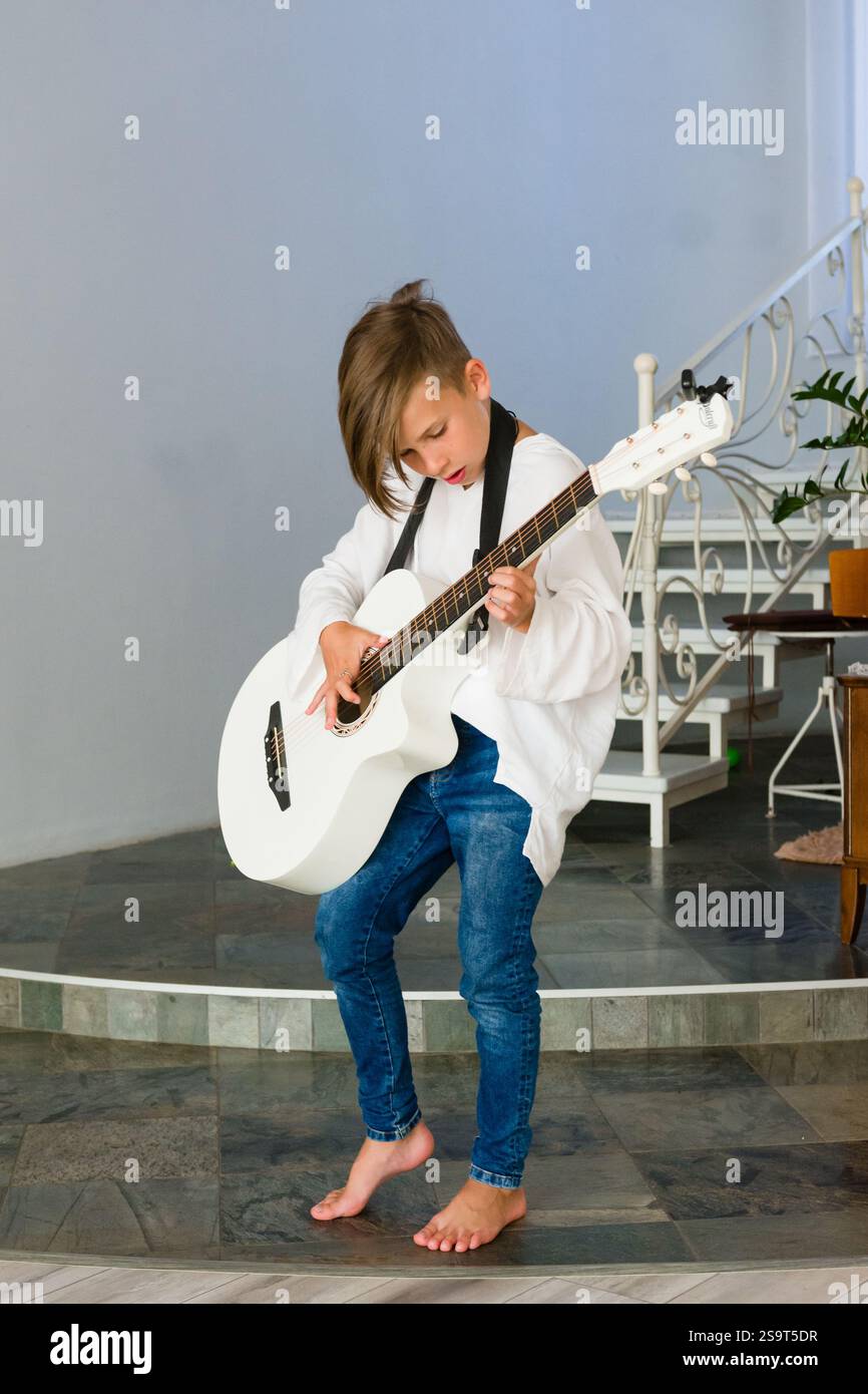 A child with shoulder-length hair plays a white acoustic guitar in a ...