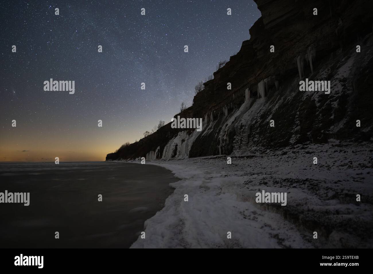 Frozen cascades on a cliff by the sea under a starry night sky. Winter ...