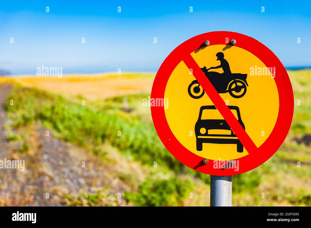 A bright red and yellow road sign prohibits motorcycles and cars, shown ...