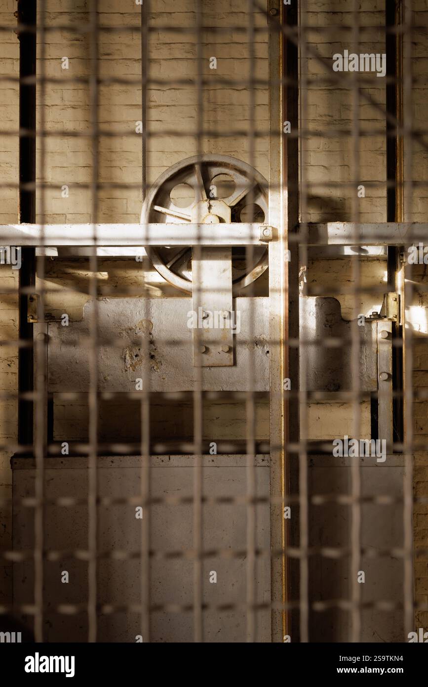 A pulley wheel and counterweight in an old, decommissioned lift, lit by ...
