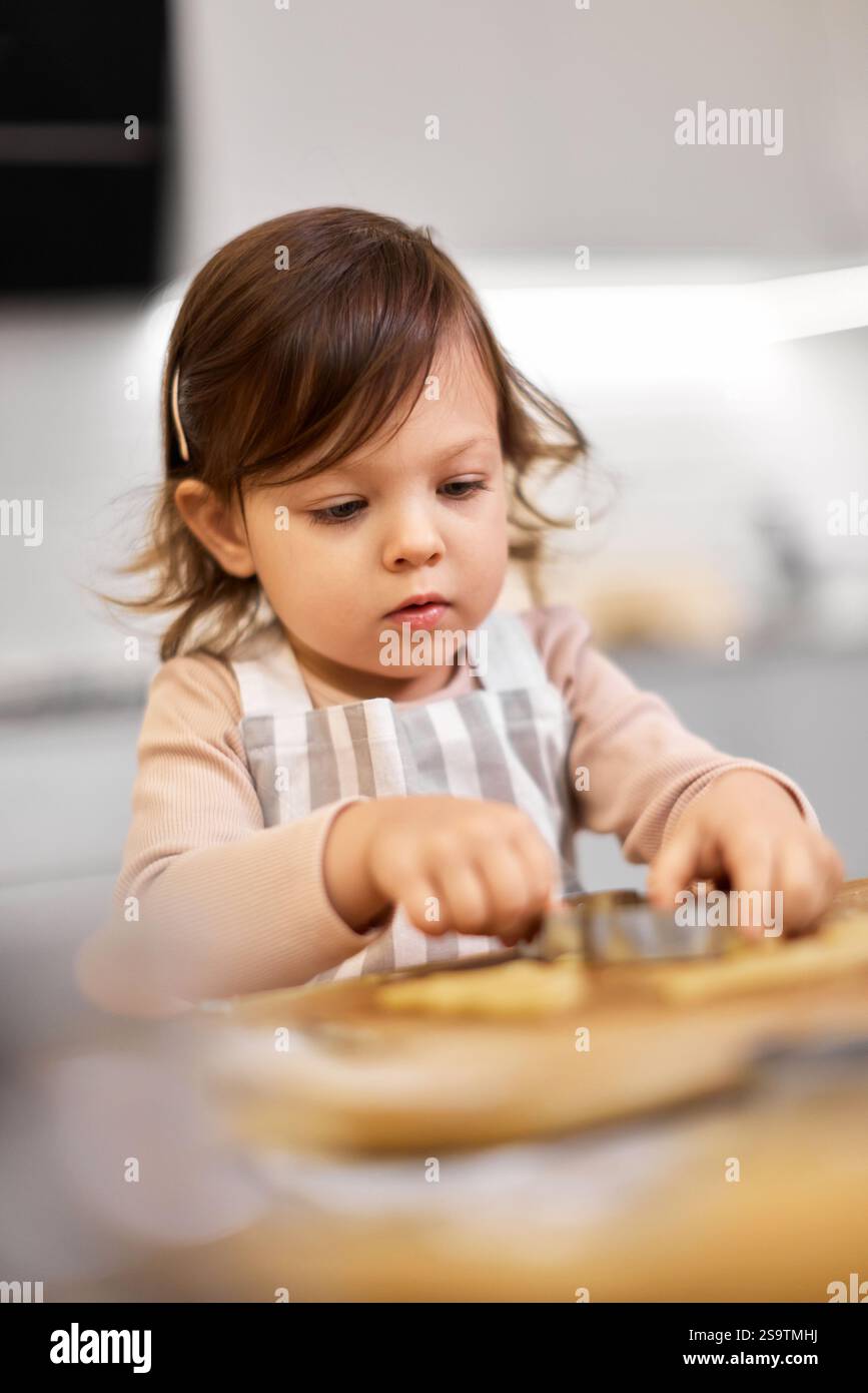 cute little child girl cutting gingerbread cookies with a cookie cutter ...
