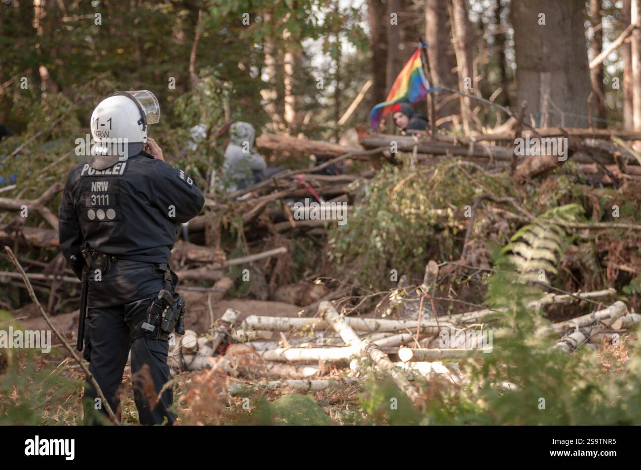 In a forest setting, a police officer stands in front of a makeshift ...