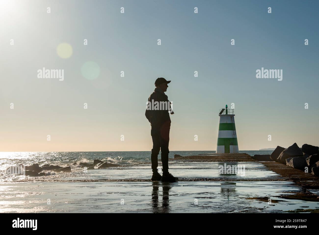silhouette of a man walking along a causeway to a lighthouse with ...