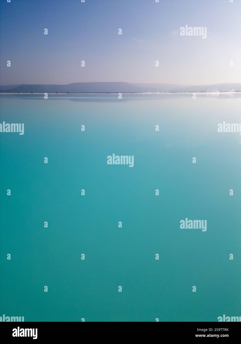 A turquoise tailings pond near a cement factory, surrounded by rugged ...