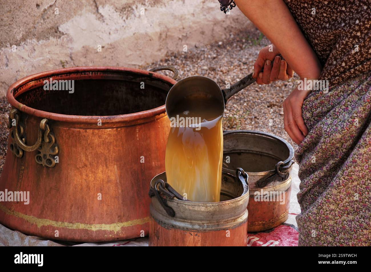 Woman pouring grape juice inside the cauldron, preparing grape molasses ...