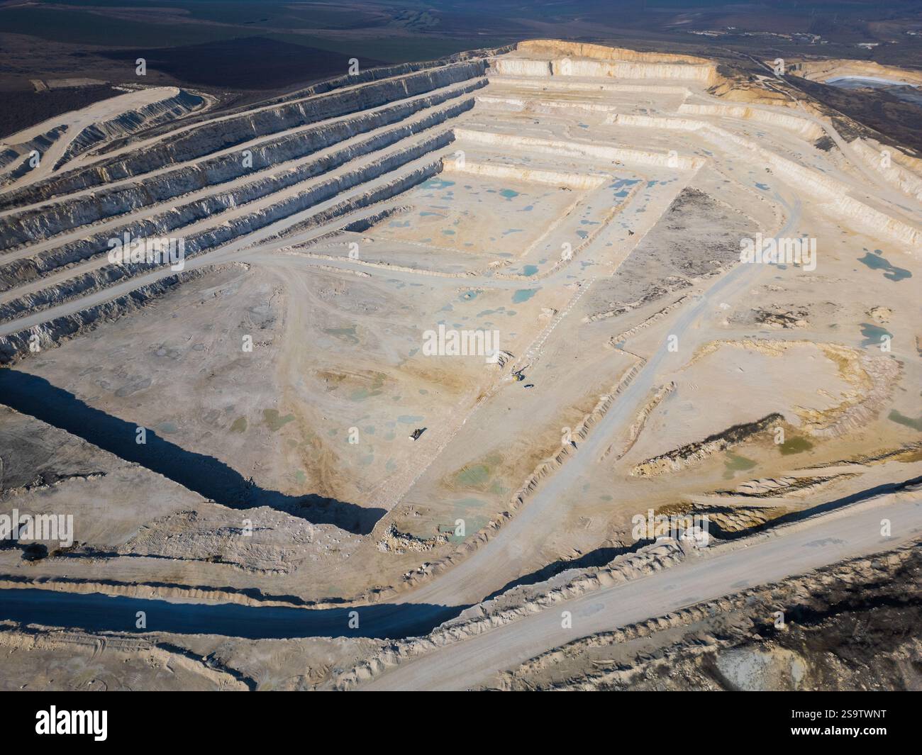 An open-pit quarry with terraced layers and heavy machinery operating ...