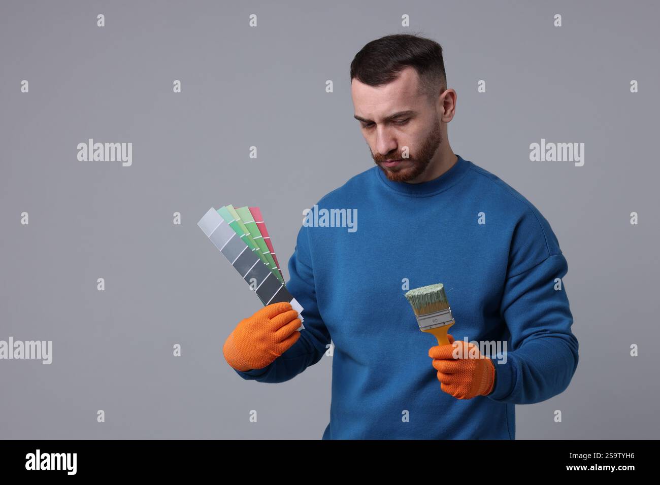 Man with paintbrush and color selection chart on light grey background ...