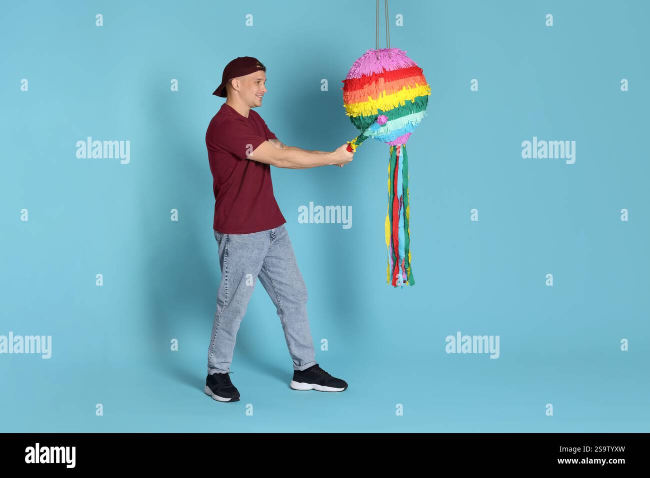 Happy man breaking pinata on light blue background Stock Photo - Alamy