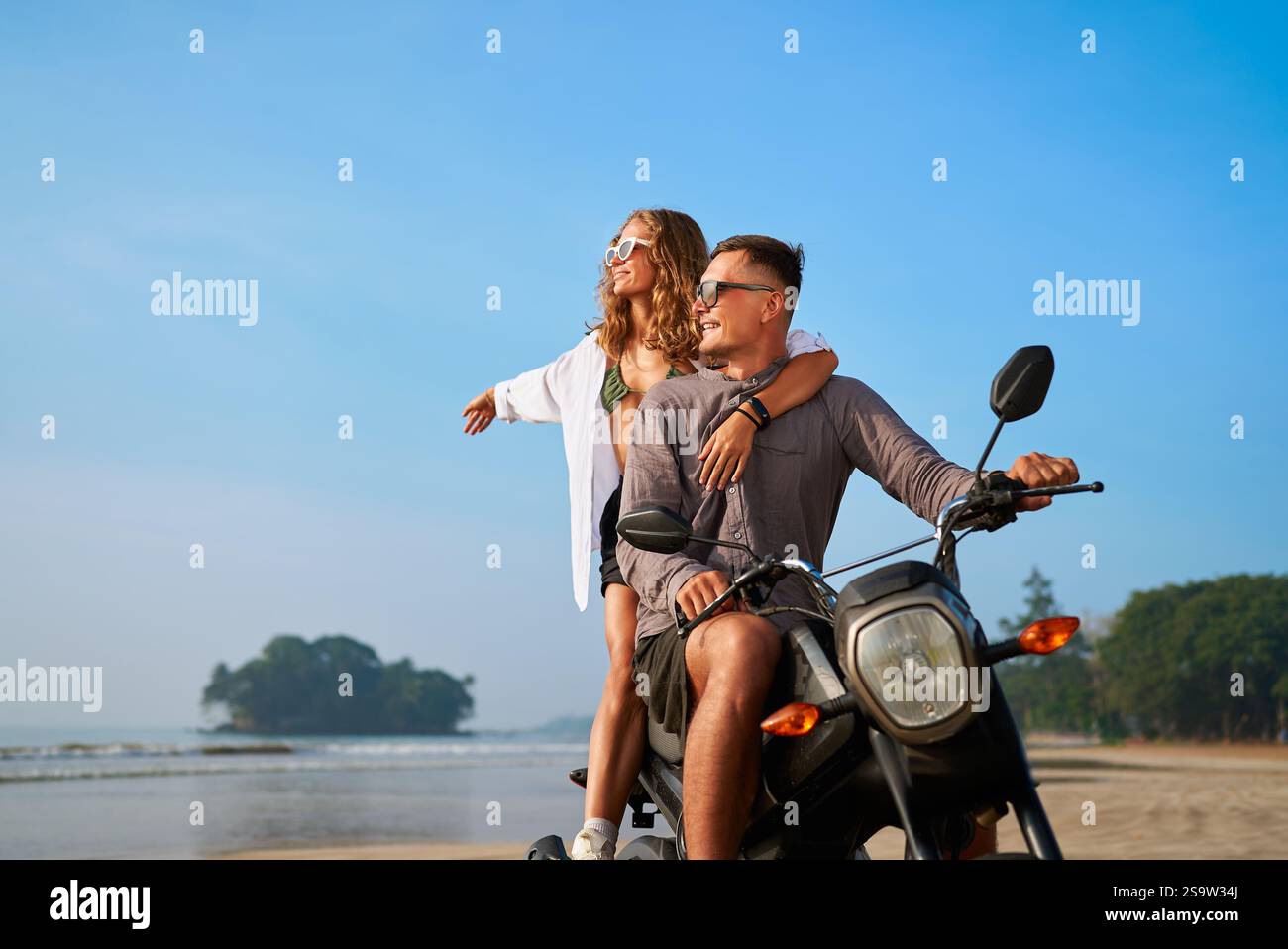 Couple rides motorbike on beach. Woman enjoying breeze, man steering ...