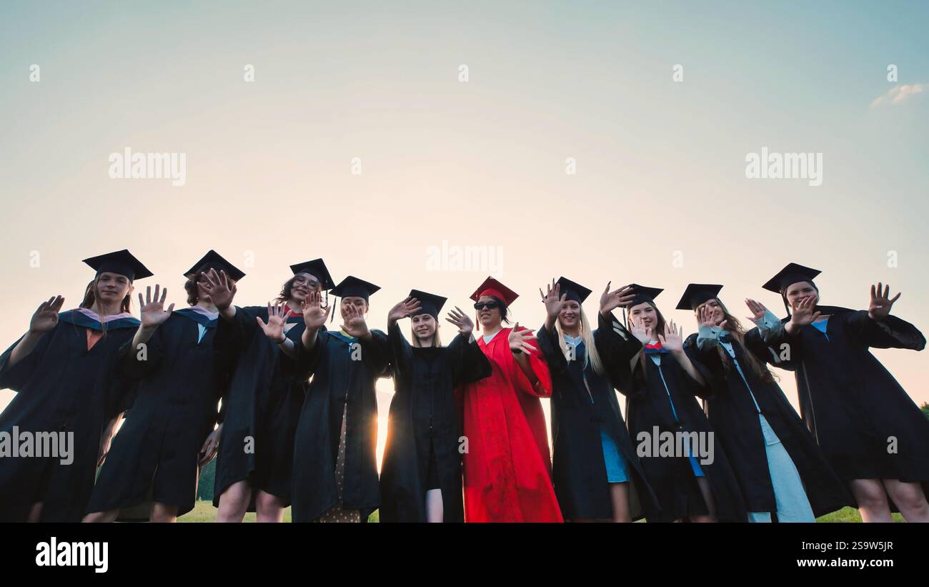 Happy students in graduation robes waving their hands at sunset Stock ...