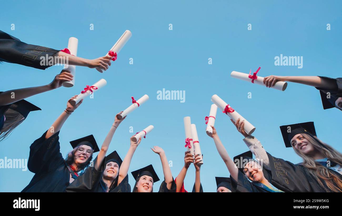 Smiling graduates joyfully raising diplomas to the sky, celebrating ...